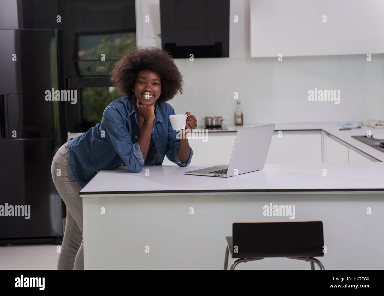 Young smiling black woman using computer and drinking coffee in modern ...