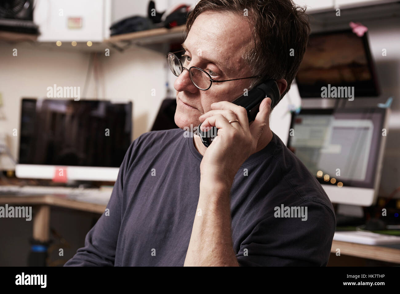 A man sitting in a room full of computers with a telephone to his ear ...