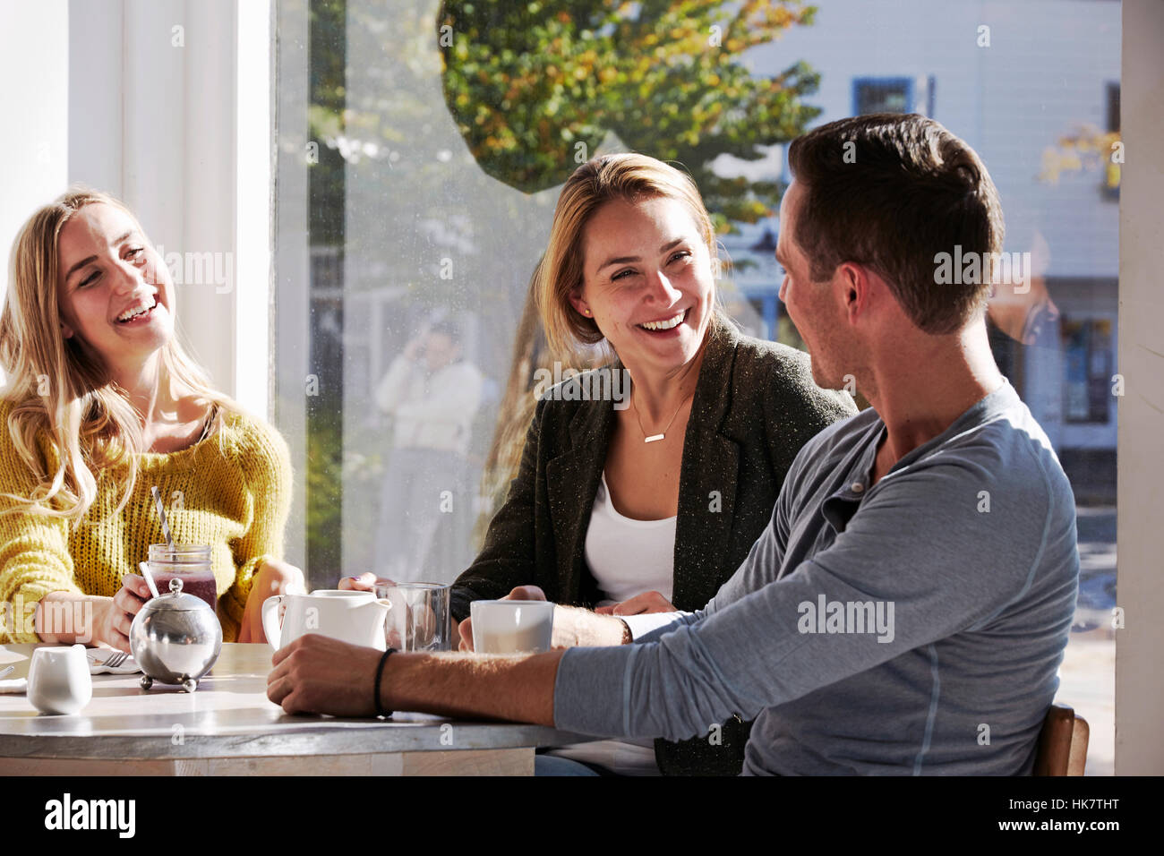 Three people sitting at a table talking, with mugs and jars of ...