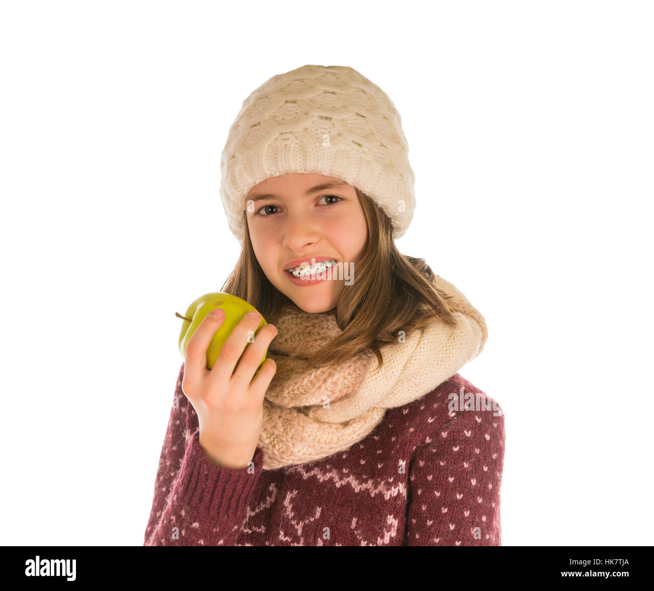 Smiling girl in warm sweater, hat, scarf and mittens eating an apple ...