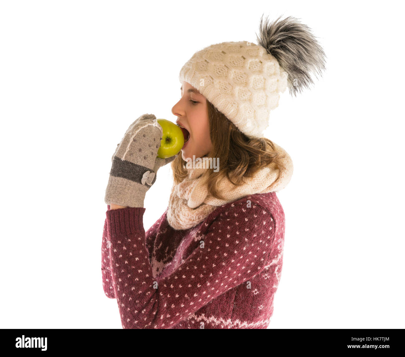 Cute girl in warm sweater, hat, scarf and mittens eating an apple ...