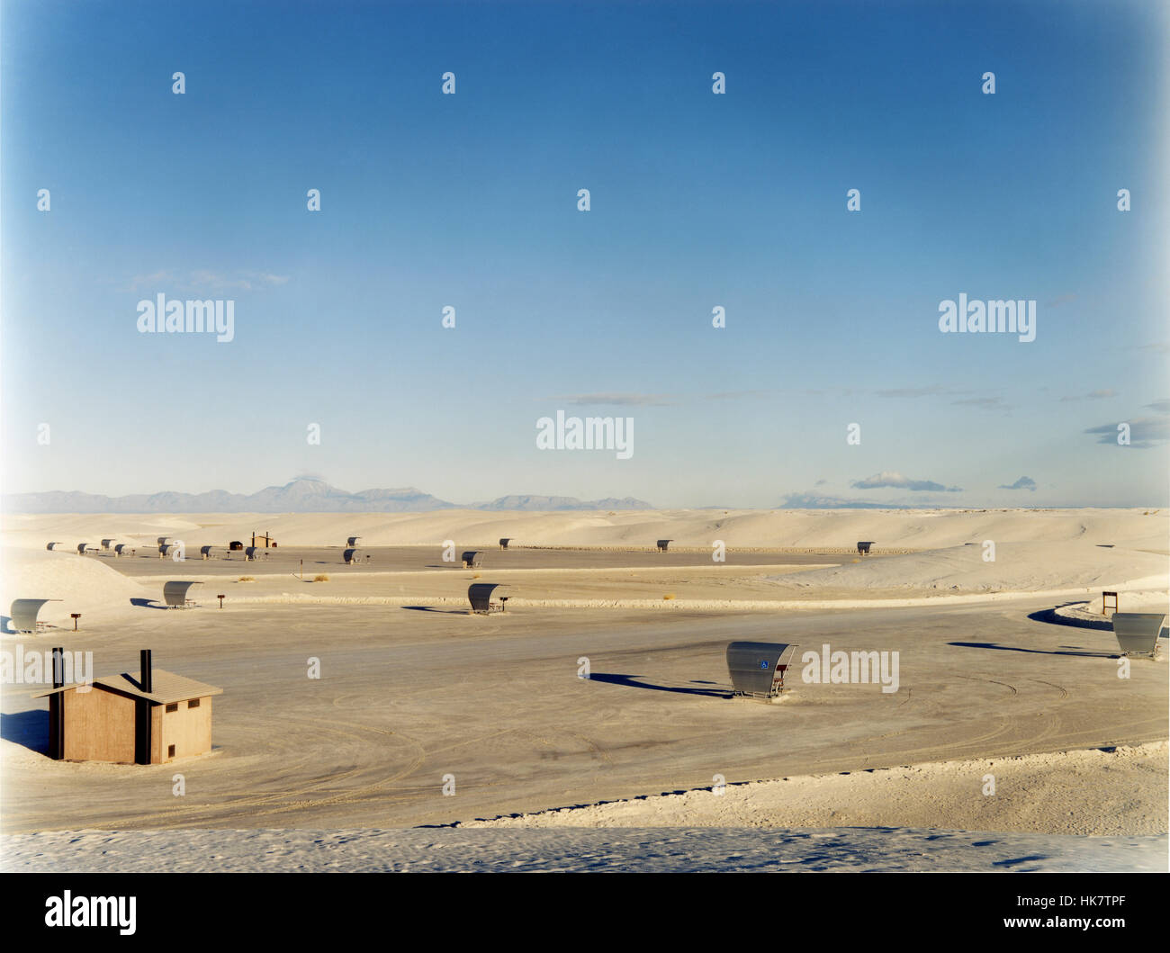 An open space a desert landscape, with a small cabin and sun shelters ...