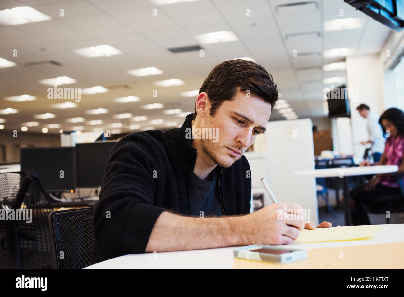 A man sitting at a table in an office writing Stock Photo - Alamy