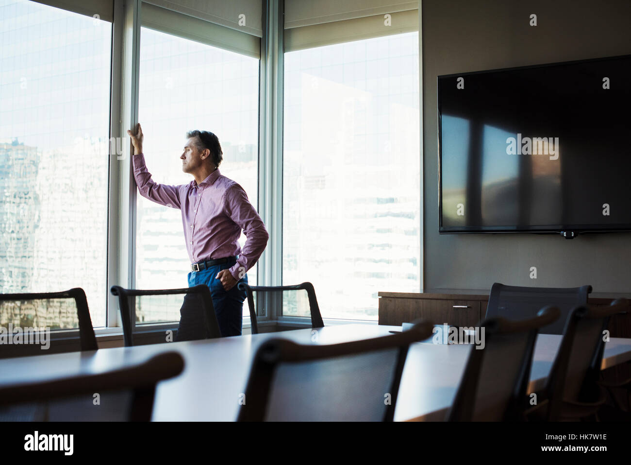 A man in a meeting room looking out of a window at an urban landscape ...