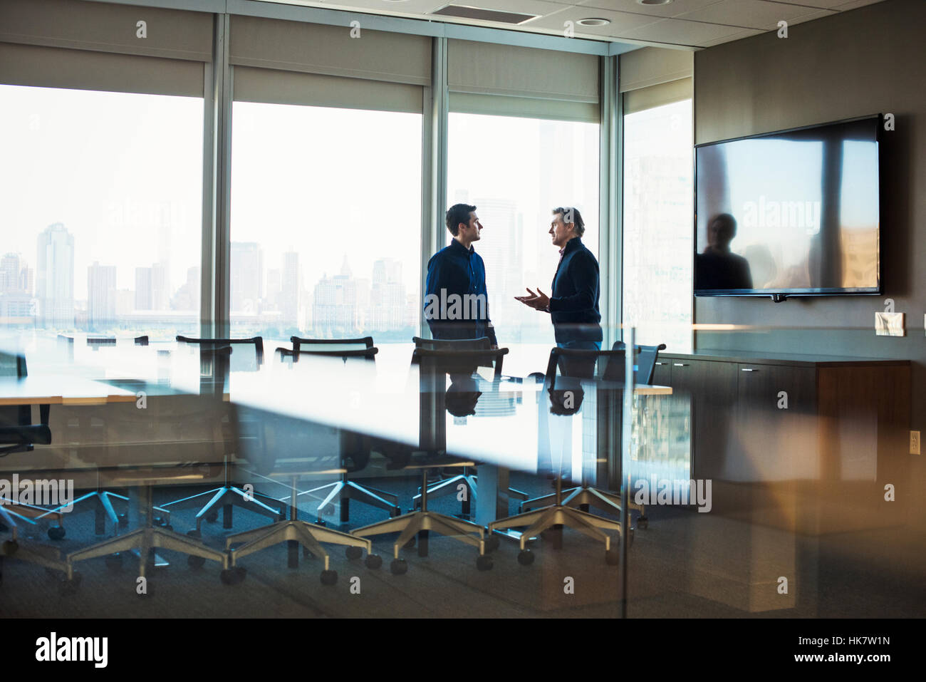 Two men standing at a table in a meeting room talking to each other ...