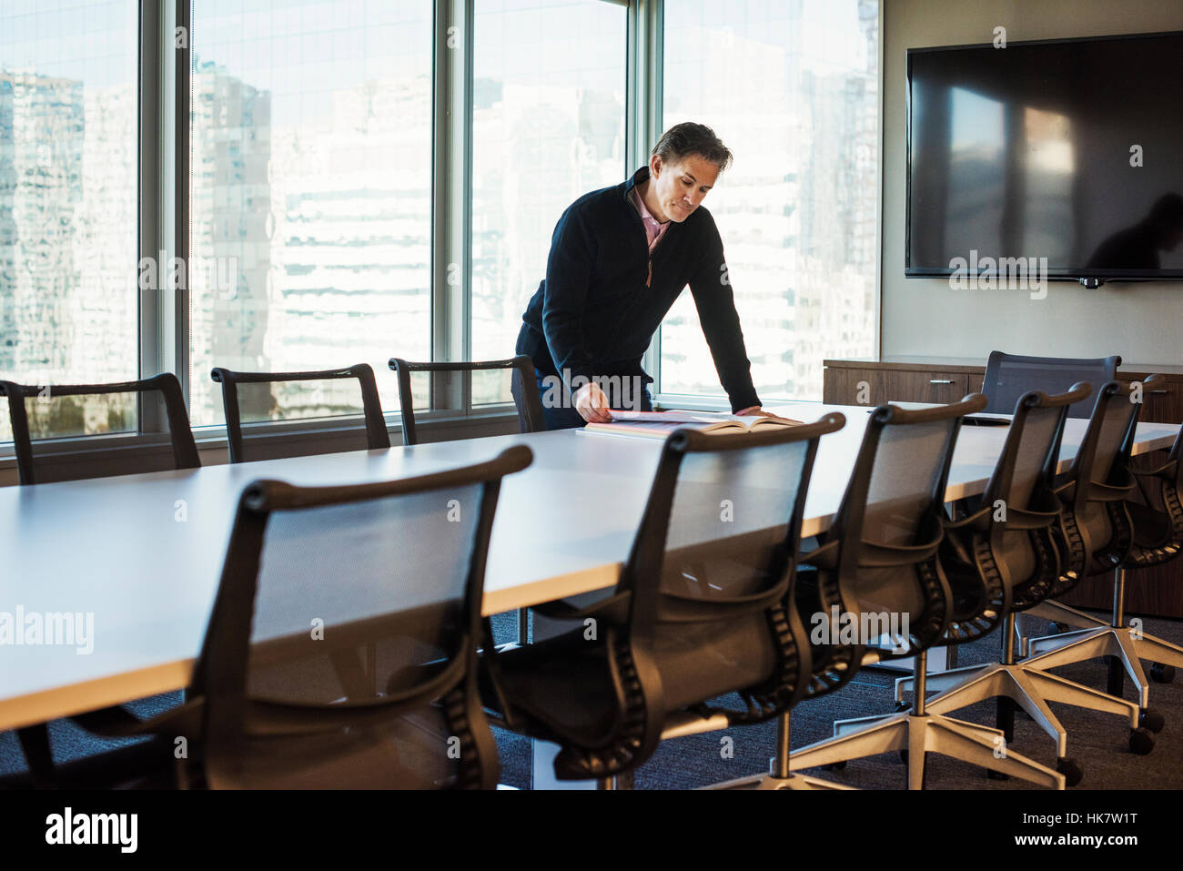 A man standing at a table in a meeting room looking down at an open ...