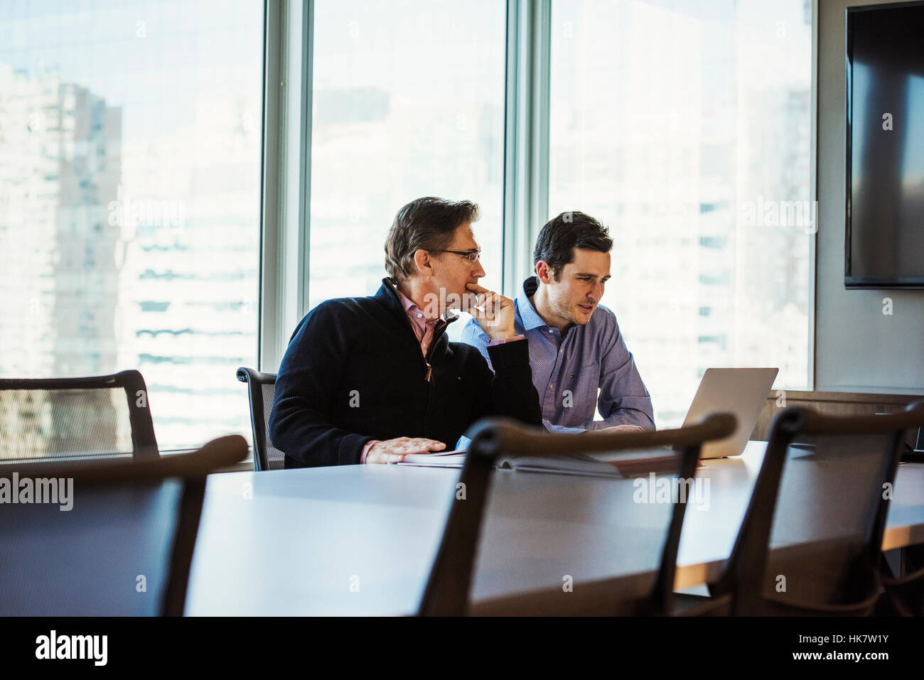Two men at a table in a meeting room looking at a laptop computer Stock ...