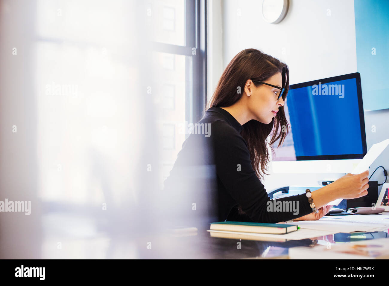 A young woman sitting at a desk in an office looking at paperwork Stock ...