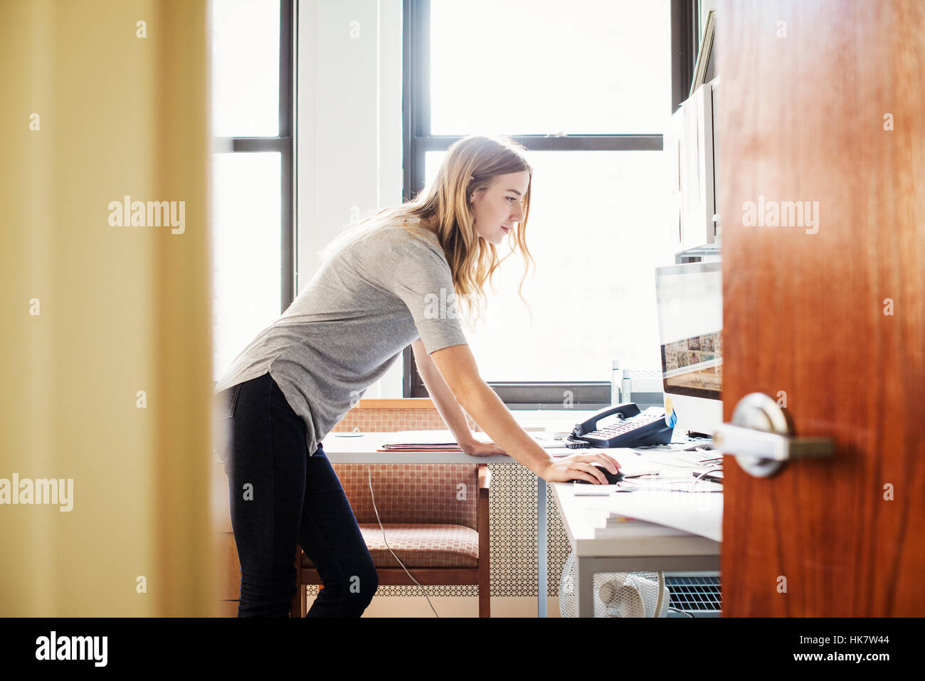 A young woman in an office standing over a desk and working at a ...