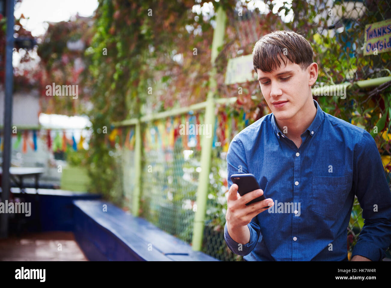 A young man sitting outdoors looking down at a cellphone Stock Photo ...