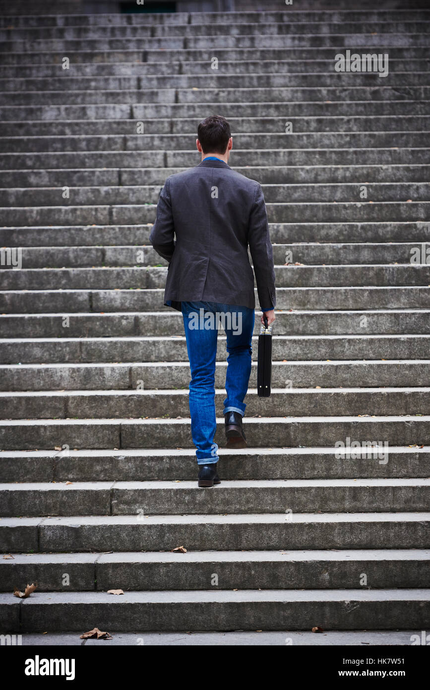 A young man walking up on a flight of steps holding a briefcase, seen ...