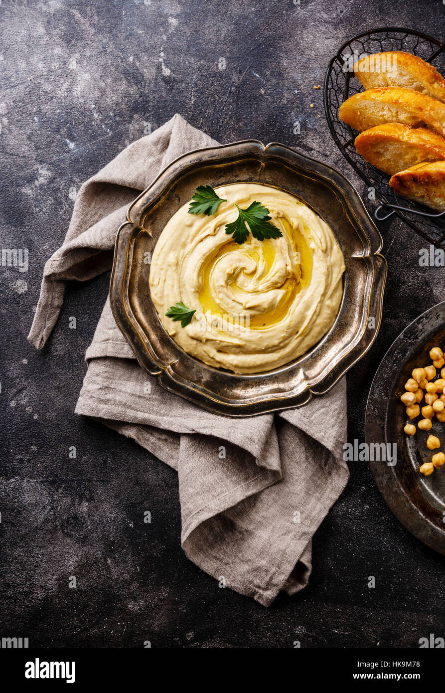 Homemade hummus with bread toasts in metal plate on black stone ...