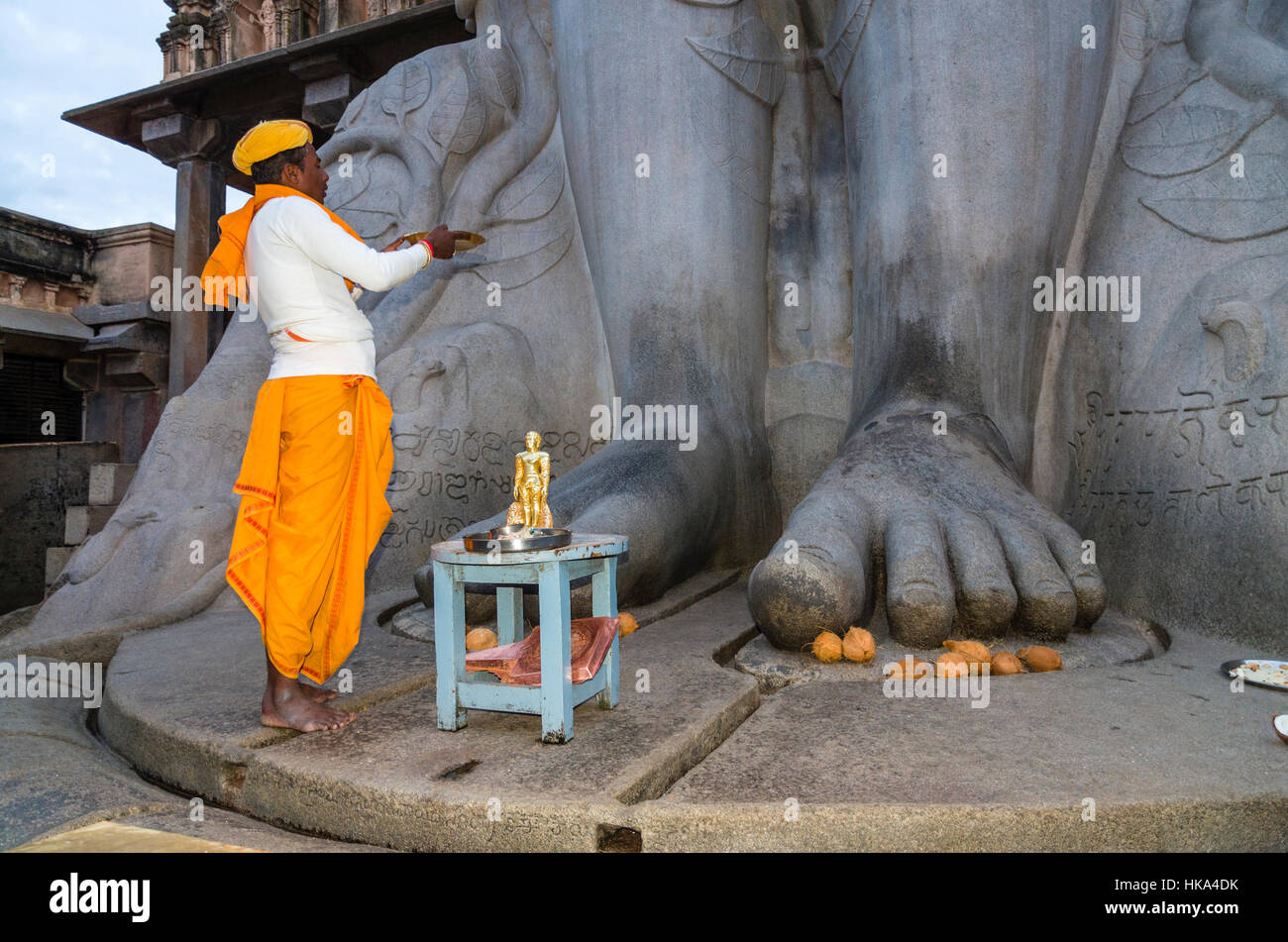 A local priest is praying at the feet of Gomateshwara, the statue of ...