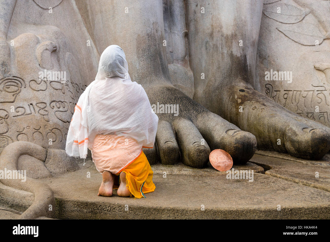 A Jain pilgrim is praying at the feet of Gomateshwara, the statue of ...