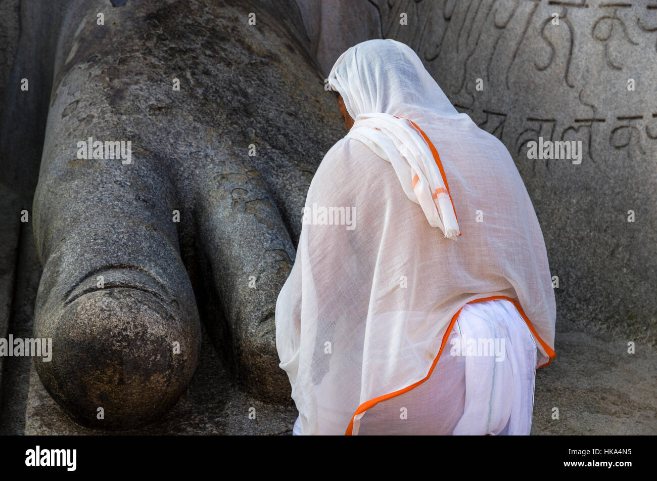 A Jain pilgrim is praying at the feet of Gomateshwara, the statue of ...