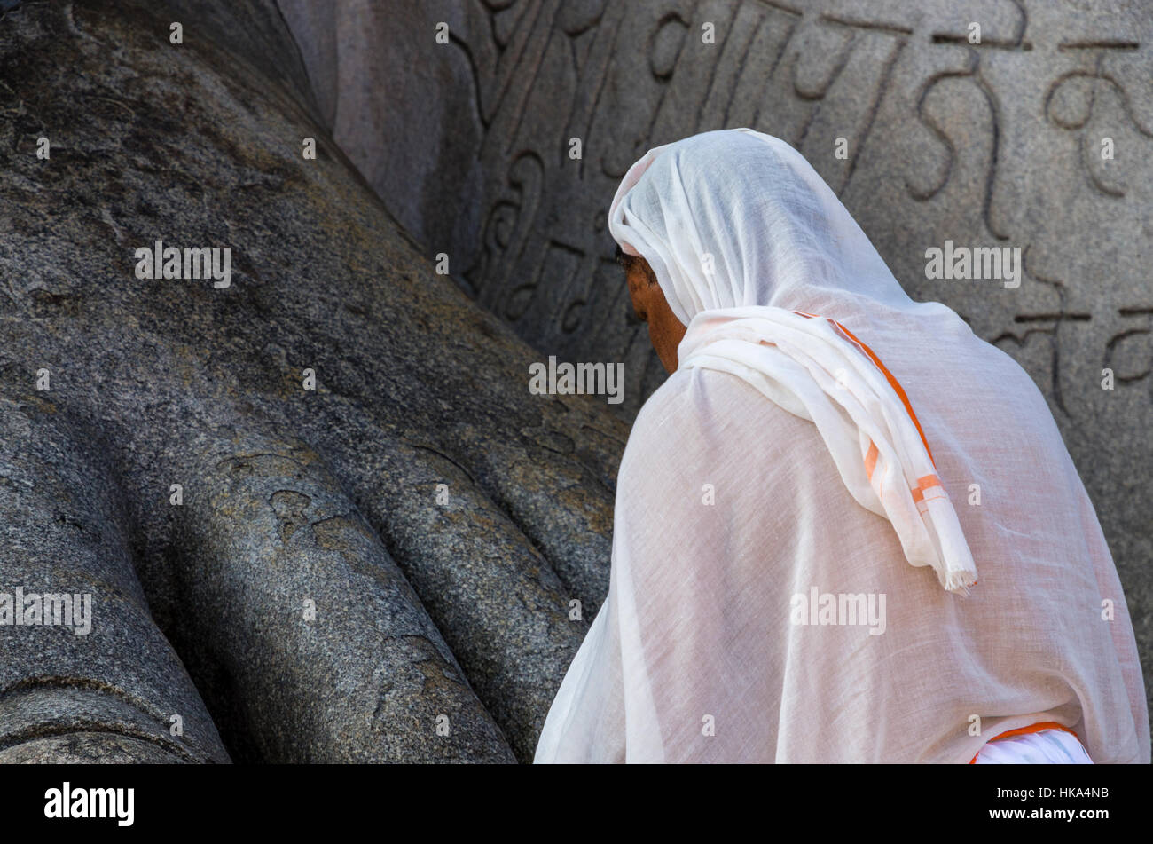 A Jain pilgrim is praying at the feet of Gomateshwara, the statue of ...