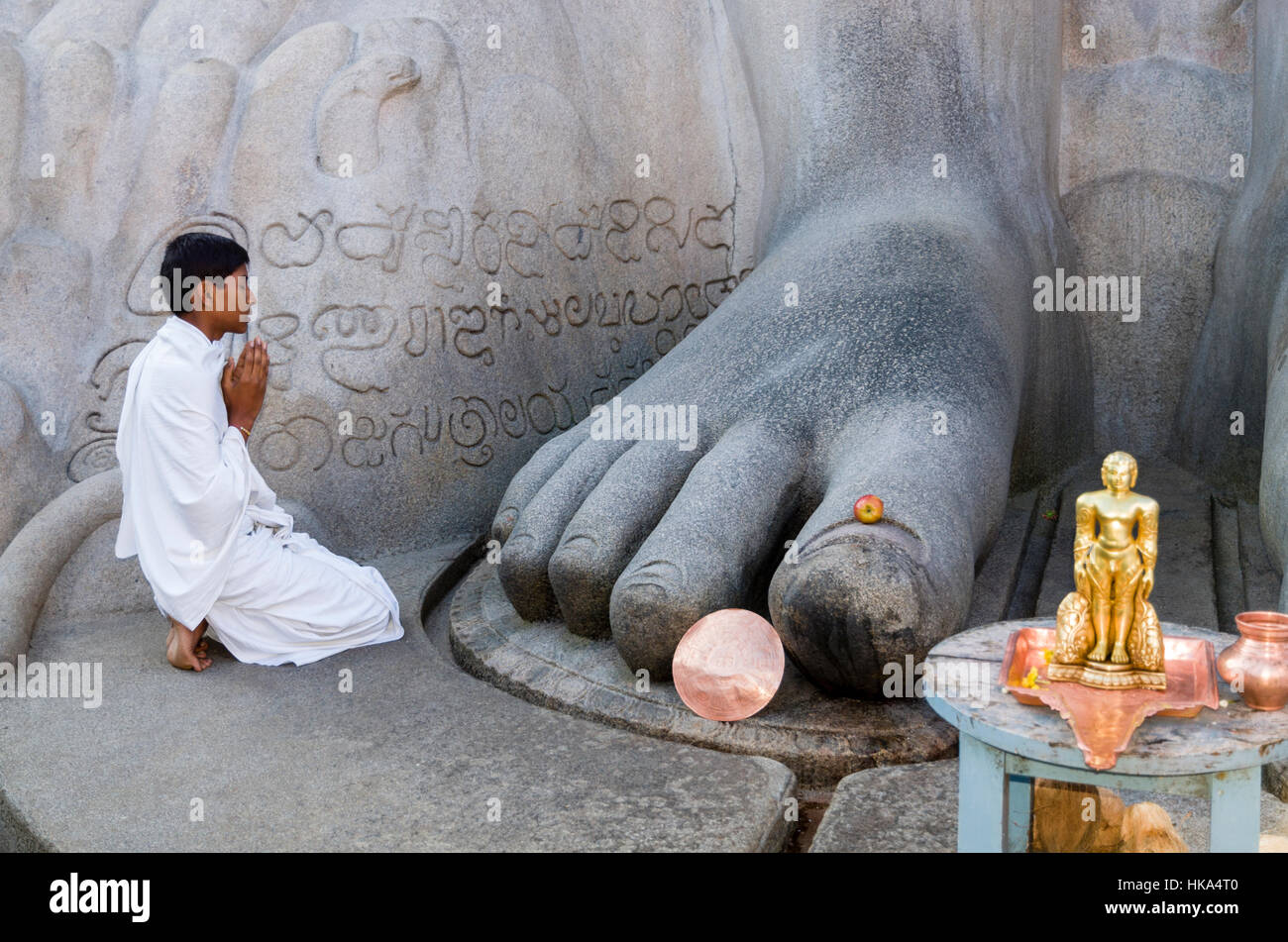 A Jain pilgrim is praying at the feet of Gomateshwara, the statue of ...