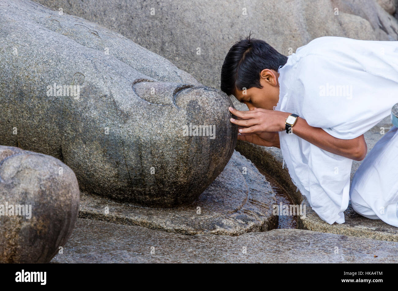 A Jain pilgrim is praying at the feet of Gomateshwara, the statue of ...