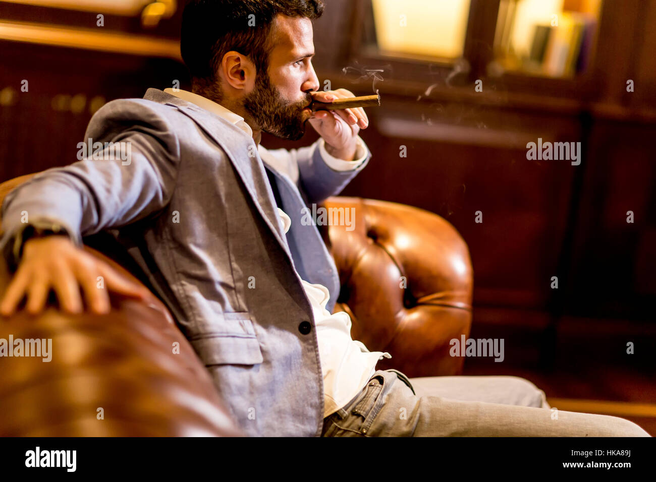 Handsome man sitting on a leather sofa and smoking cigar Stock Photo ...