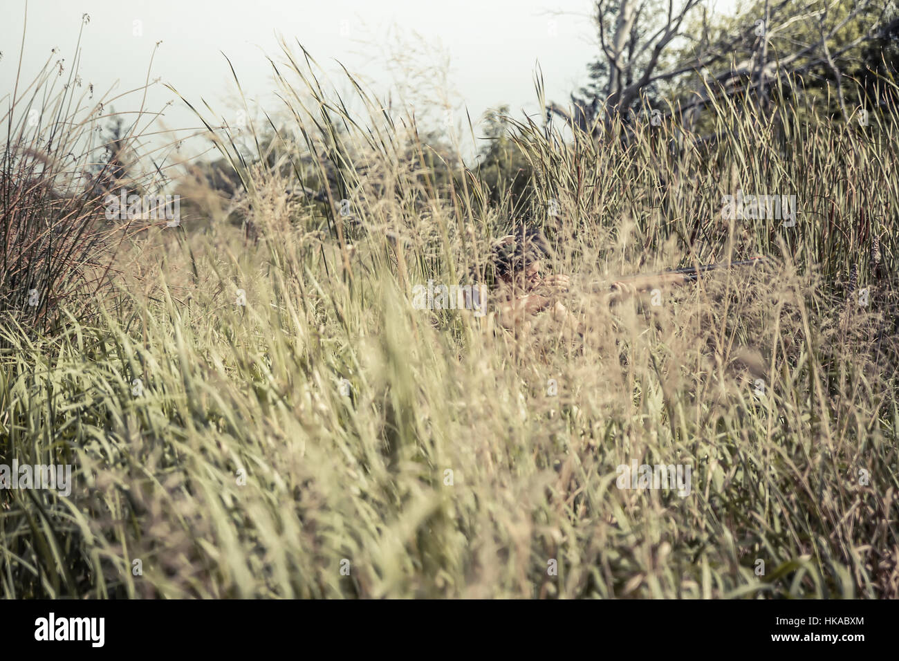 Hunting scene with hunter man aiming in tall grass in ambush with ...