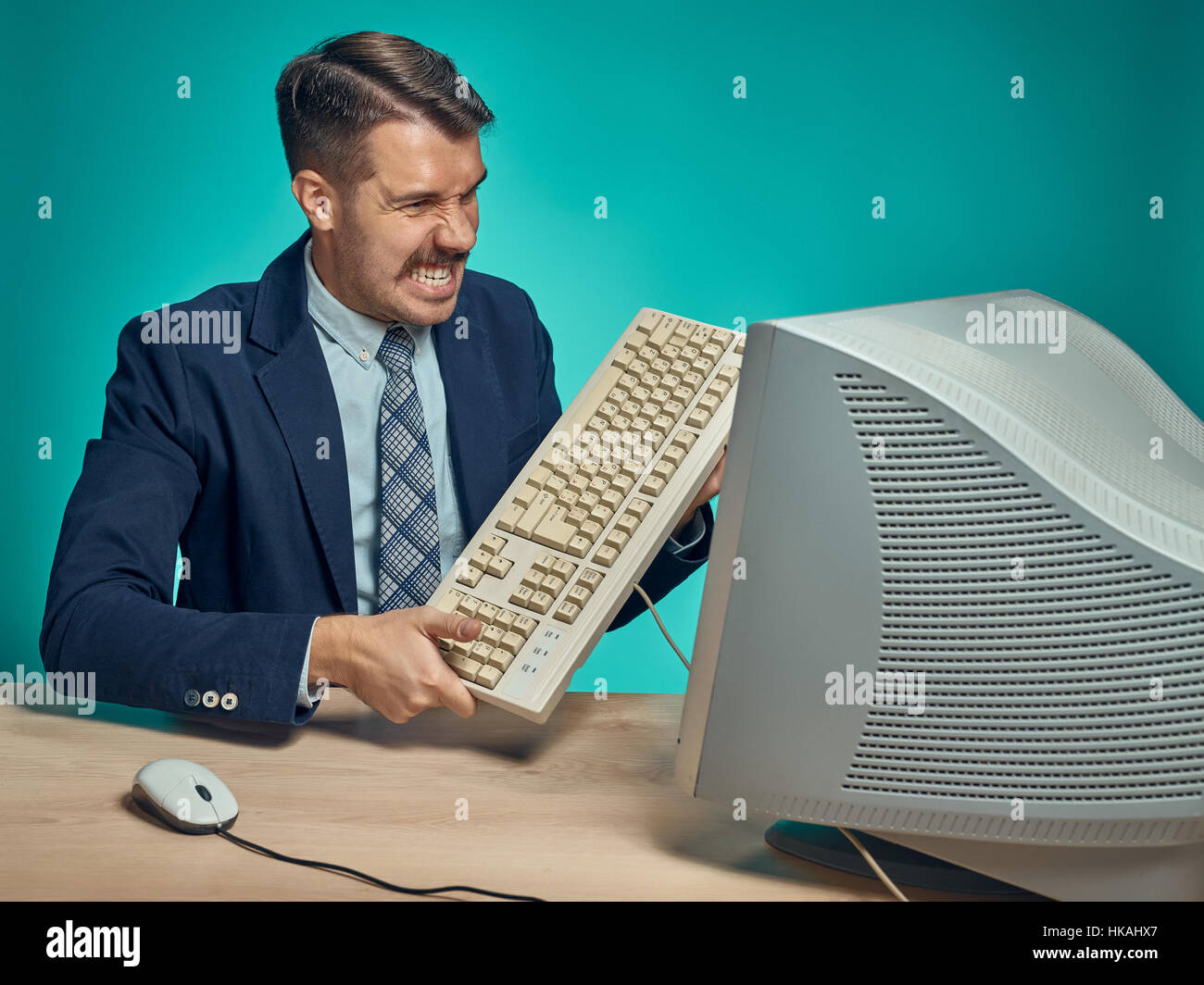Angry businessman breaking keyboard against blue background Stock Photo ...