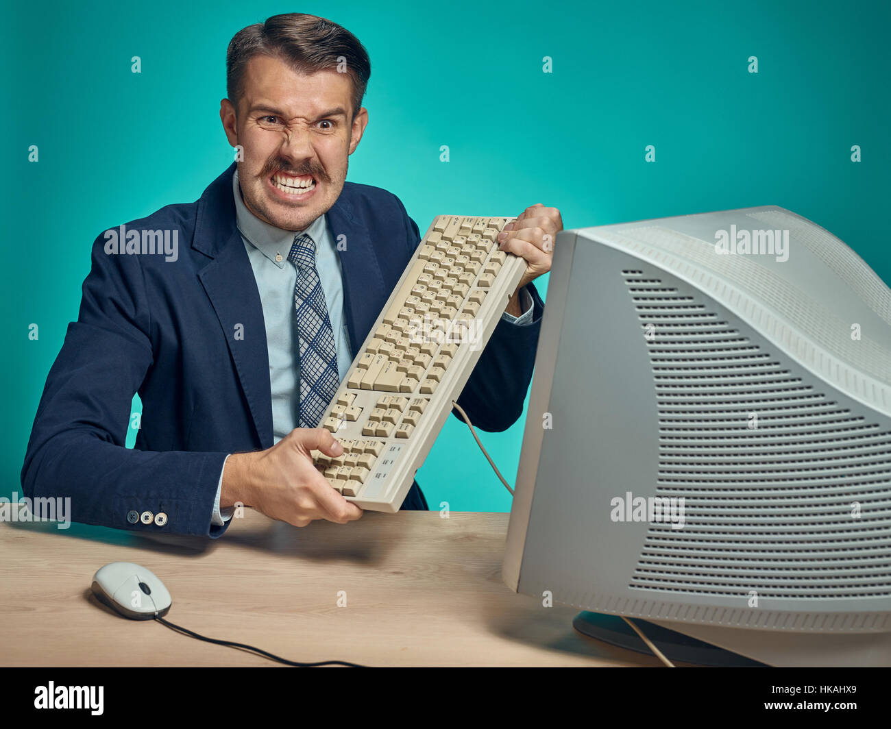 Angry businessman breaking keyboard against blue background Stock Photo ...