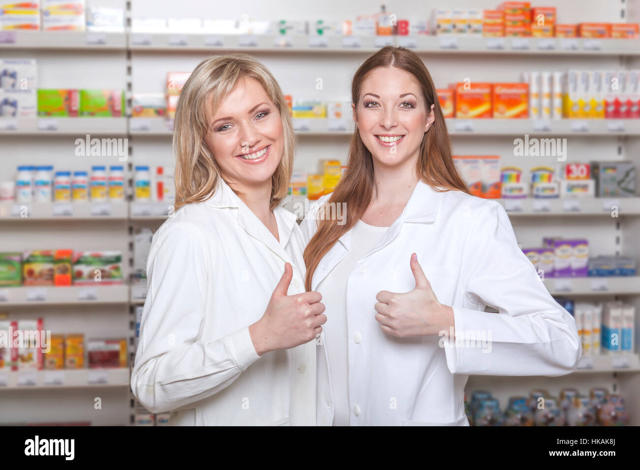 Two friendly smiling pharmacists show thumbs up in pharmacy environment ...