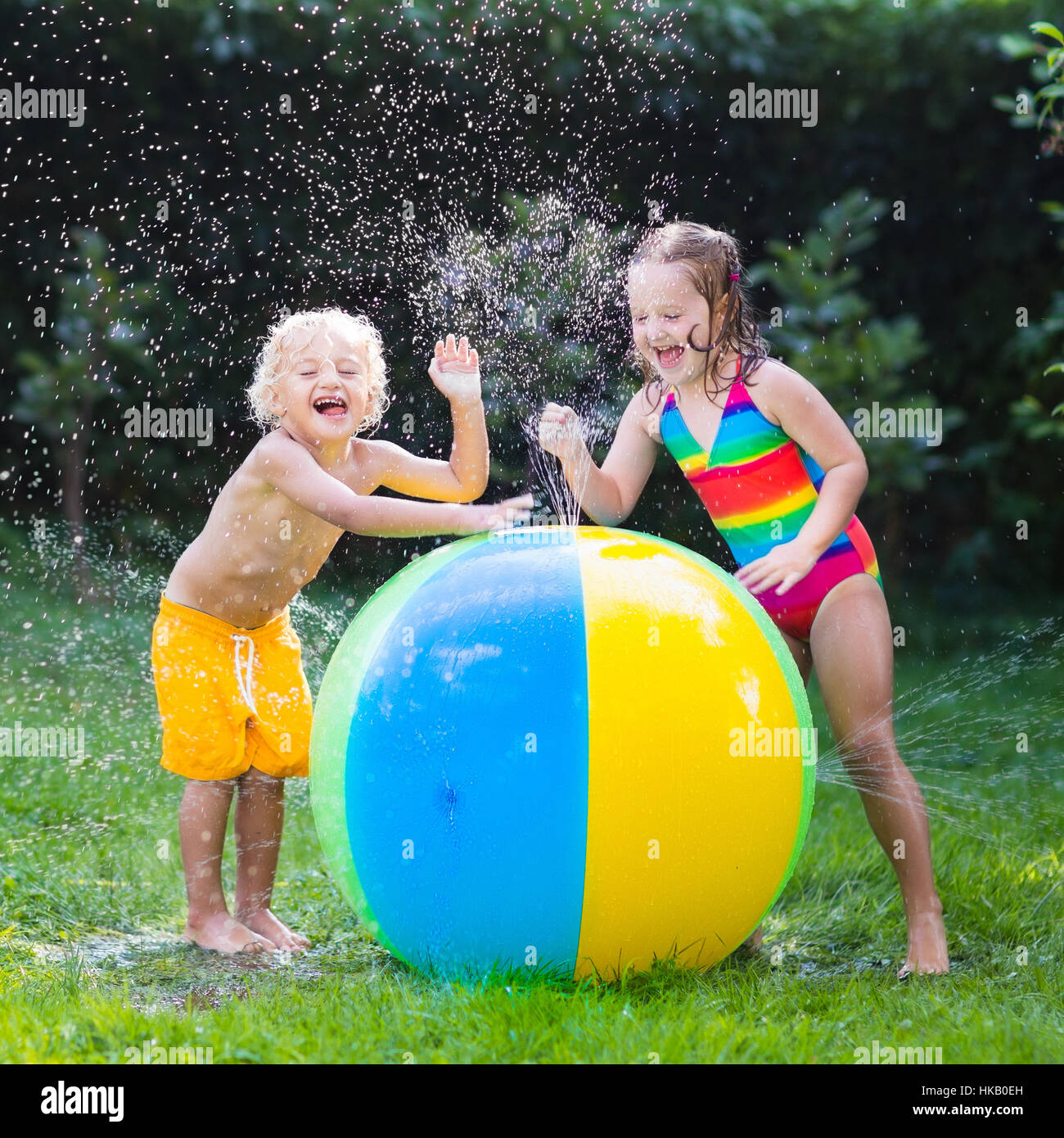 Child playing with toy ball garden sprinkler. Preschooler kid run and ...