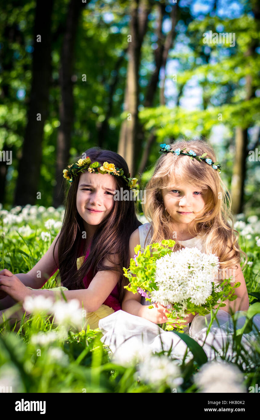 two beautiful friends sitting in green spring meadow with white flowers ...