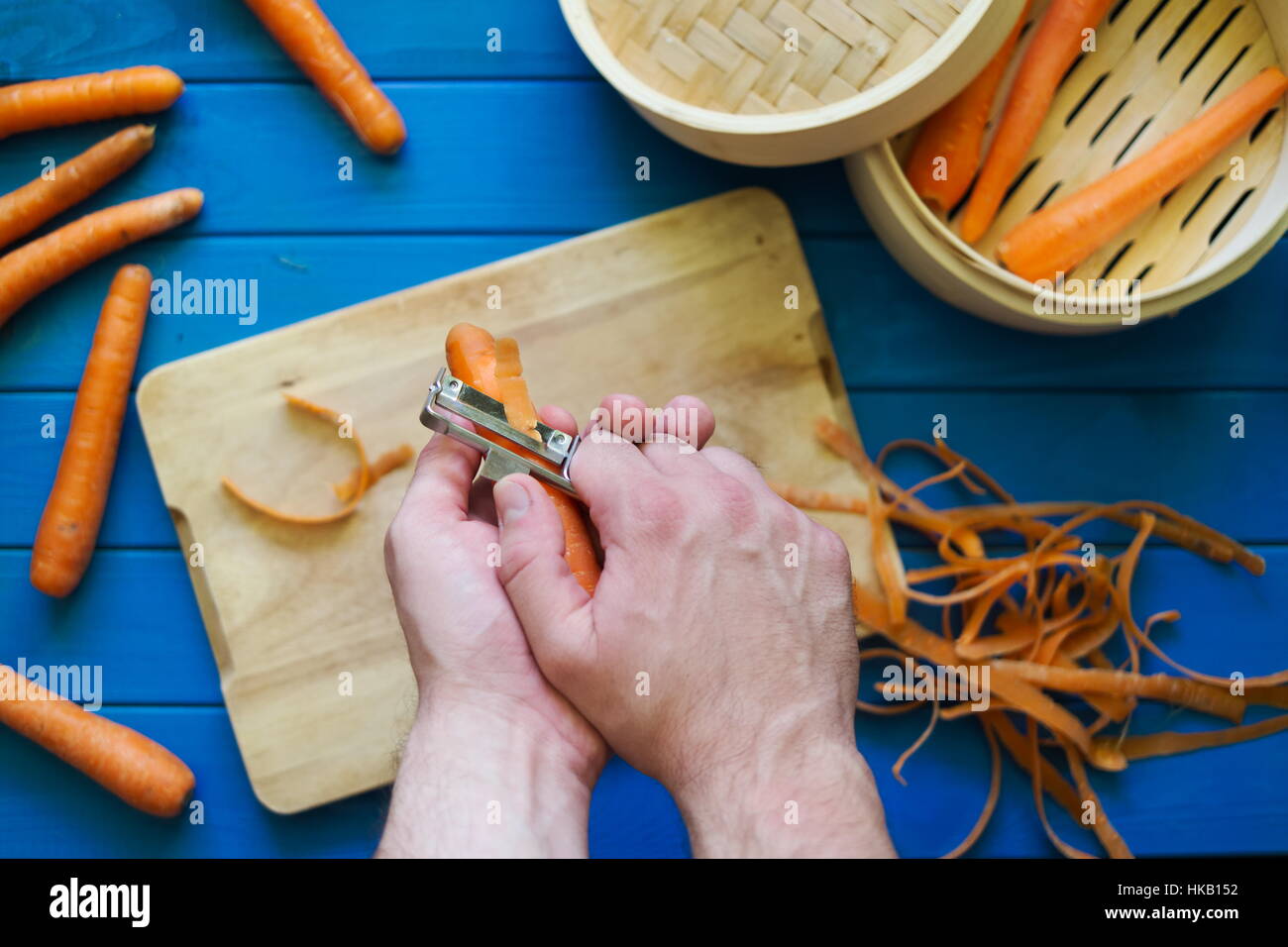 Male hands peeling an orange carrot on blue background. Concept of ...