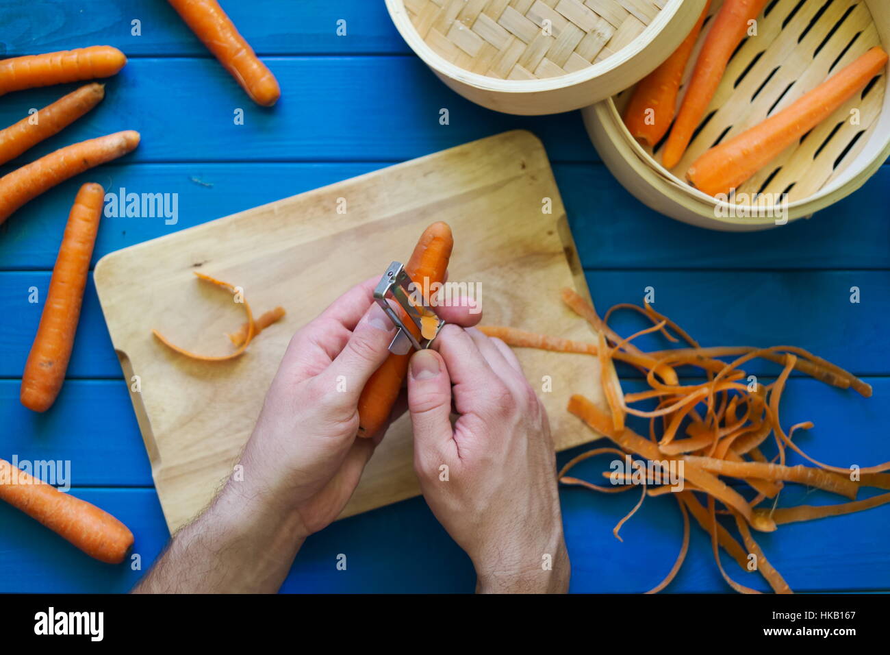 Male hands peeling an orange carrot on blue background. Concept of ...