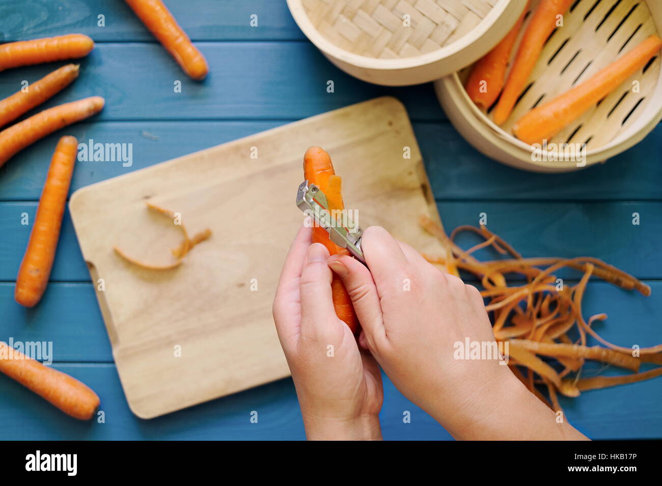 female hands peeling an orange carrot on blue background. Concept of ...