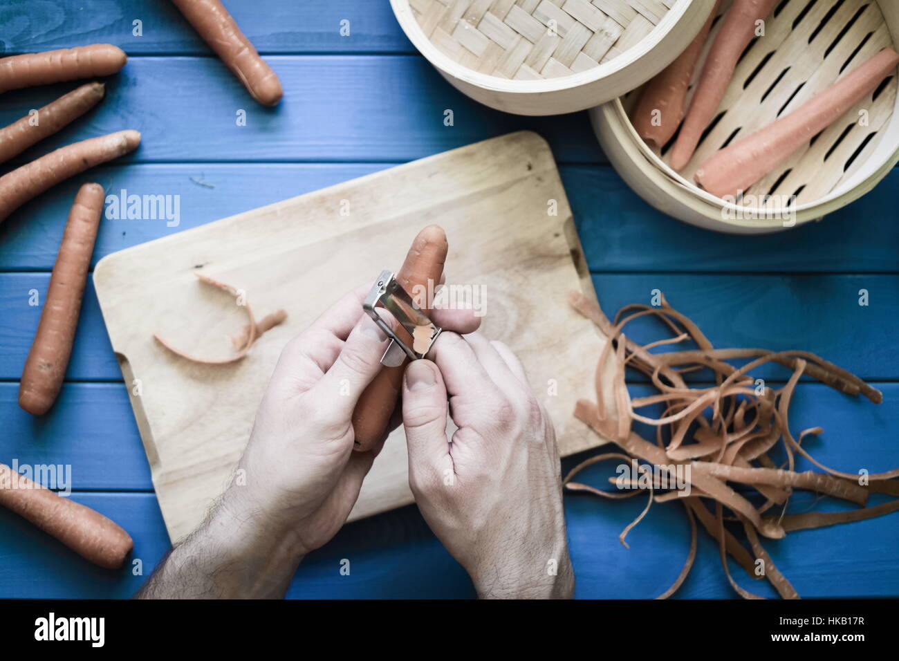 Male hands peeling an orange carrot on blue background. Concept of ...