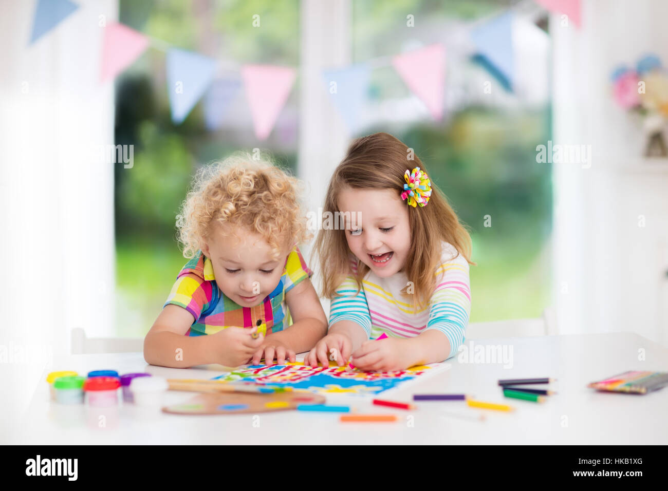 Little boy and girl draw together in white room with window. Kids doing ...