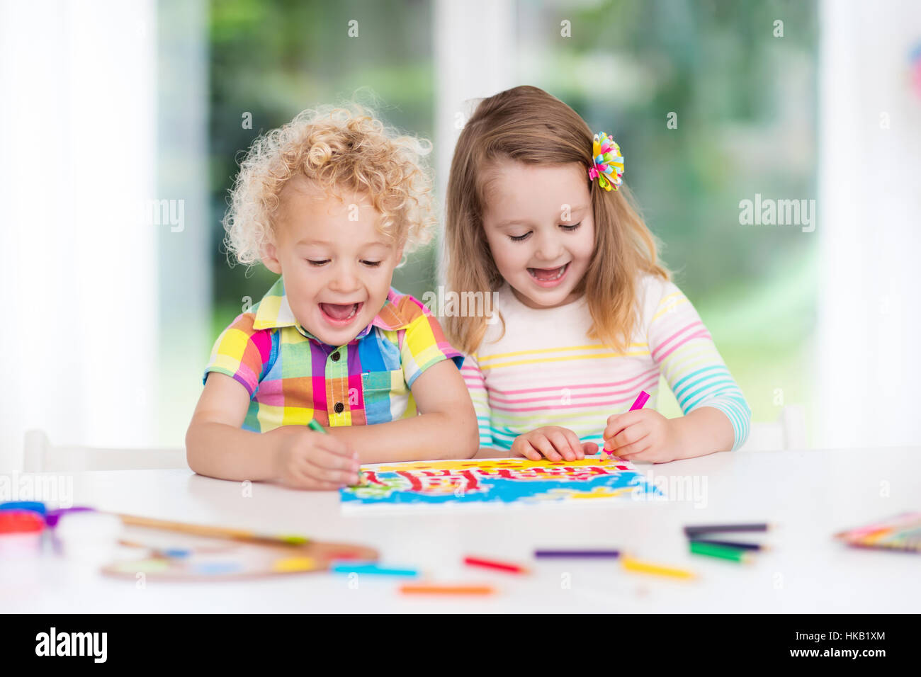 Little boy and girl draw together in white room with window. Kids doing ...