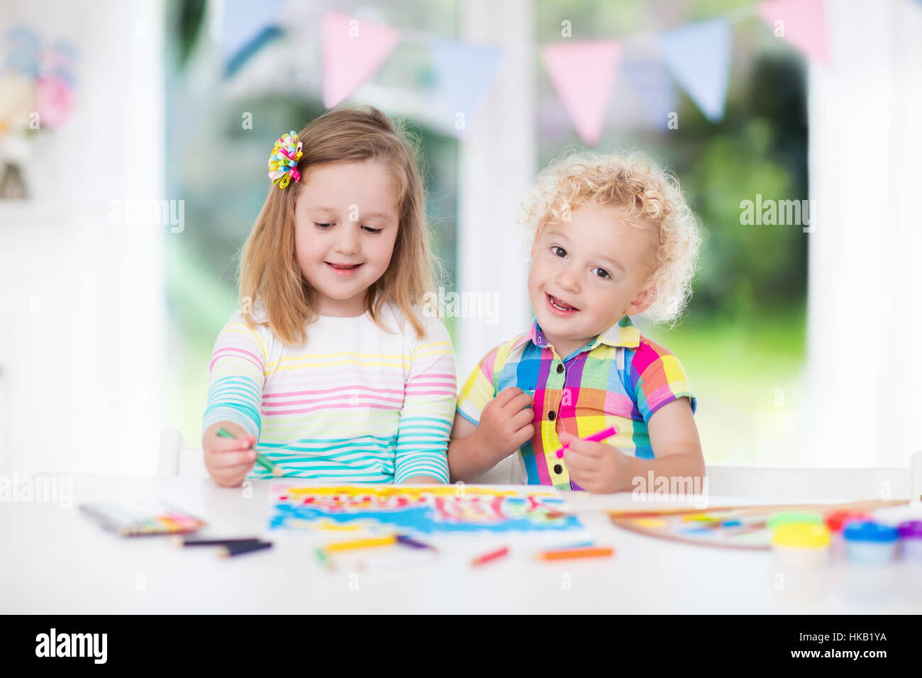 Little boy and girl draw together in white room with window. Kids doing ...