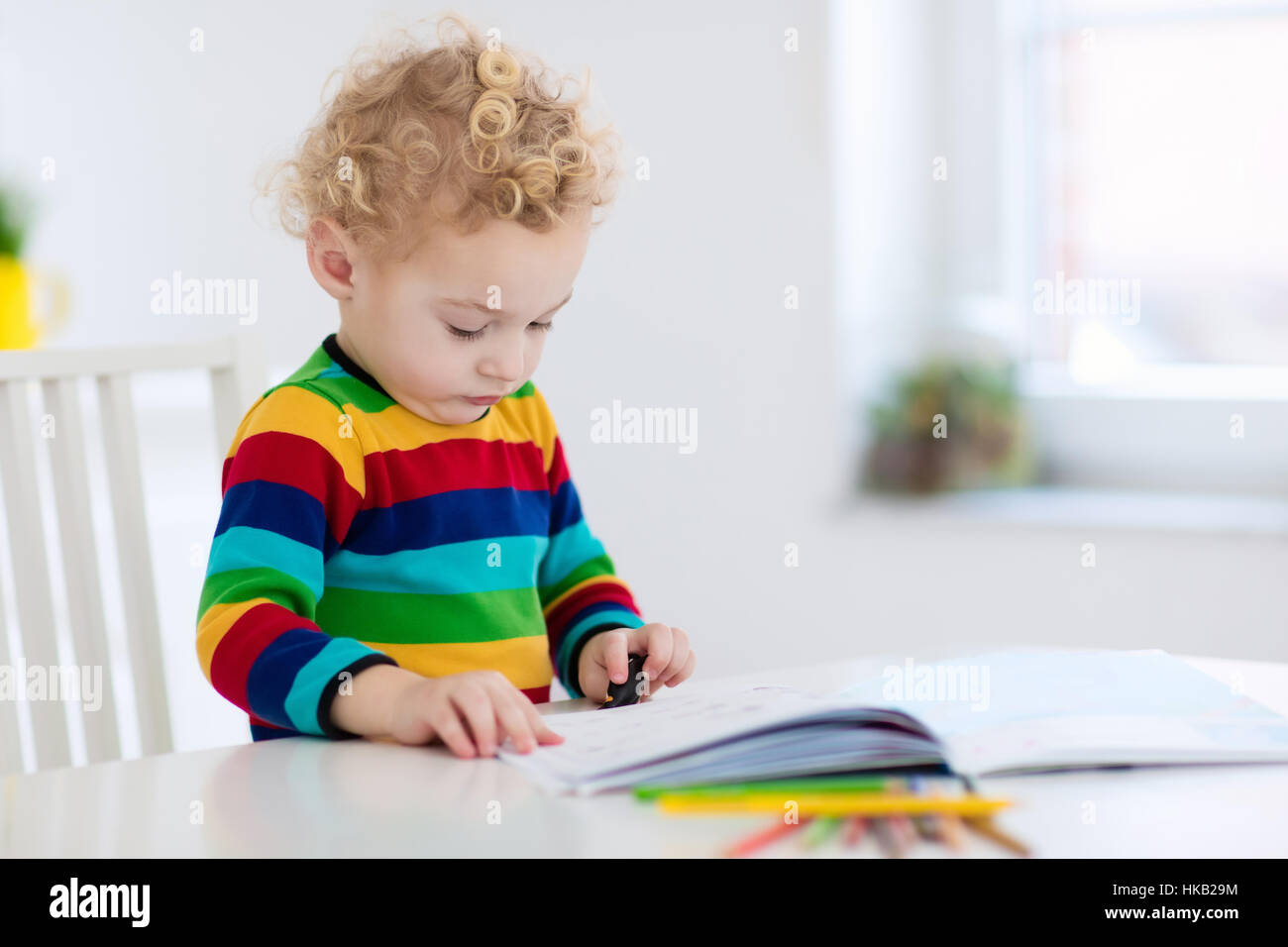 Cute little boy doing homework, reading a book, coloring pages, writing ...