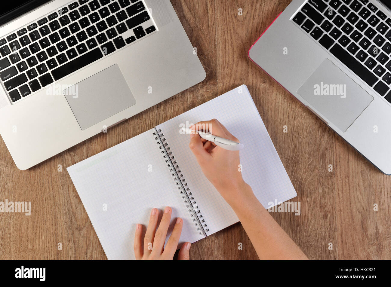 person writing in notebook infront of two laptops Stock Photo - Alamy