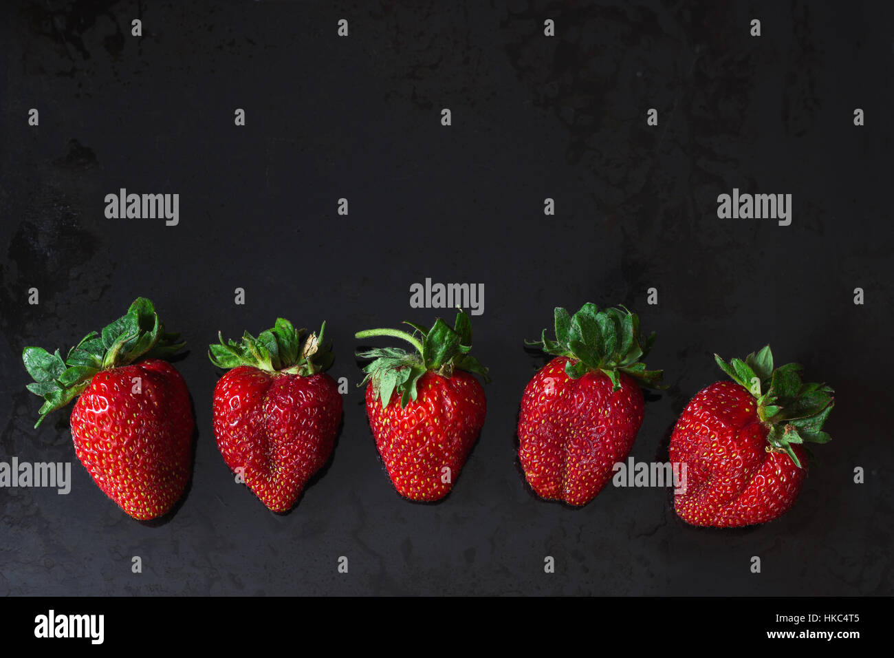 Five red strawberries in a row over black distressed reflecting ...