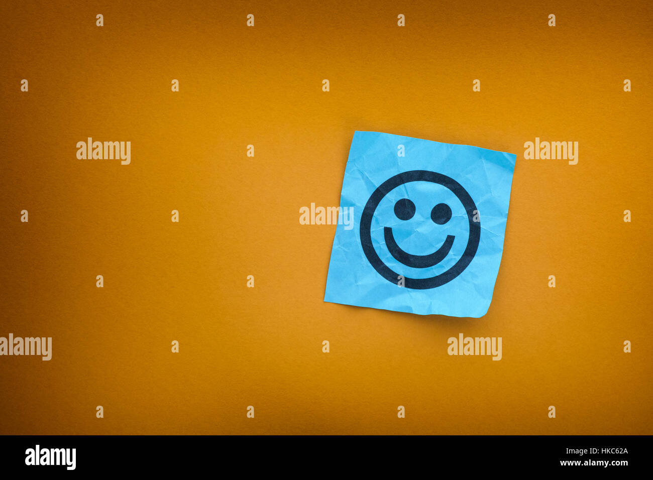 Blue paper note with happy face on a yellow paper background. Close up ...