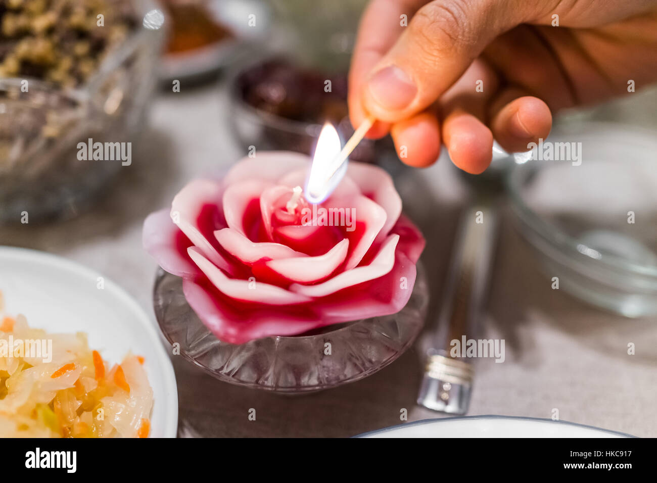 Hand lighting rose flower candle with match stick in glass bowl on ...