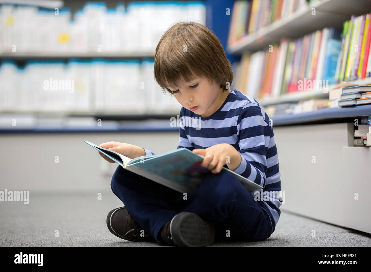 Adorable little child, boy, sitting in a book store, reading books ...