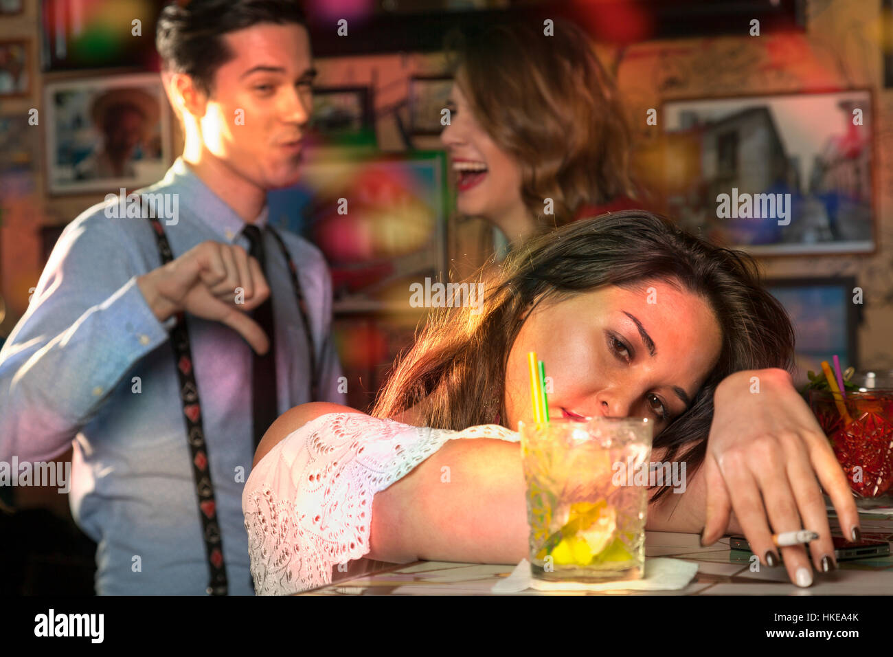 Woman lays her head on the arm as she stands at the bar and smokes a ...