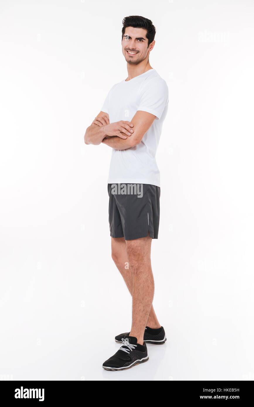 Full length portrait of a smiling sports man standing with arms folded ...