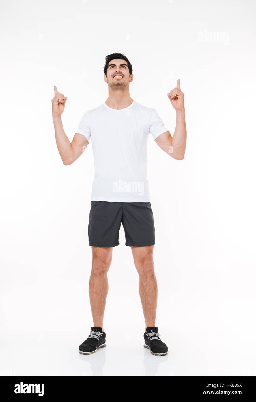 Full length portrait of a smiling sports man pointing fingers up over ...