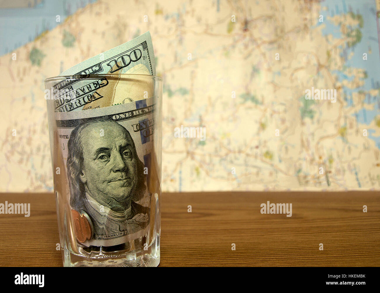 Glass as moneybox with cash savings on wooden table and map as ...