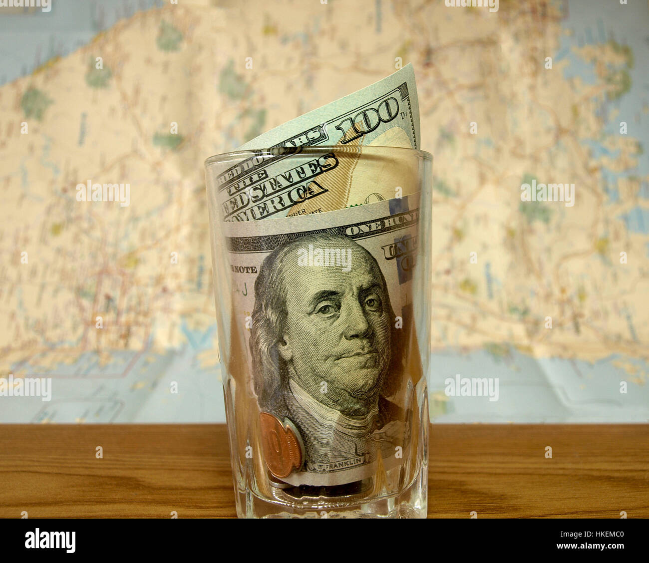 Glass of money with cash savings on wooden table and map as background ...