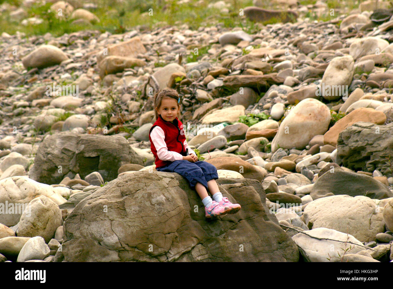 Little girl sitting on large rock in the middle of rocky landscape ...