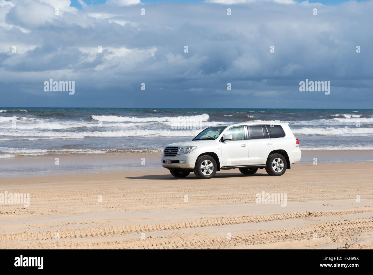 A white 4WD car driving down 75 Mile Beach on Fraser Island, Queensland ...