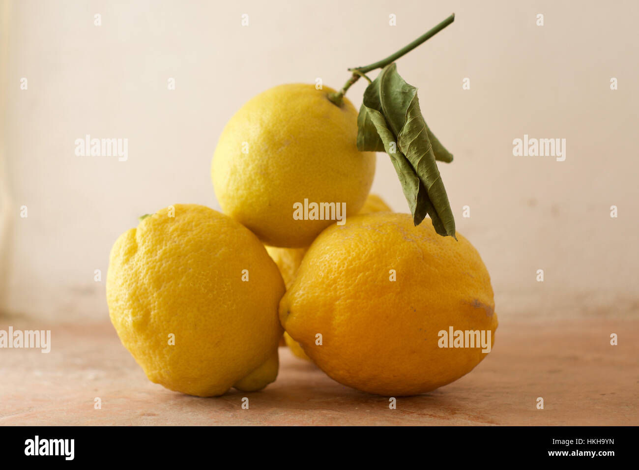 A stack of four lemons with some foliage against a rustic background ...
